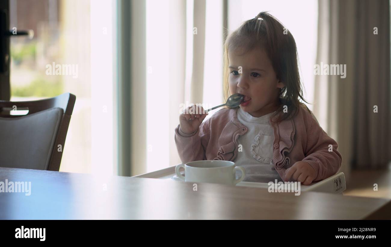 Closeup of young baby in white feeding high chair, kid is trying to eat ...