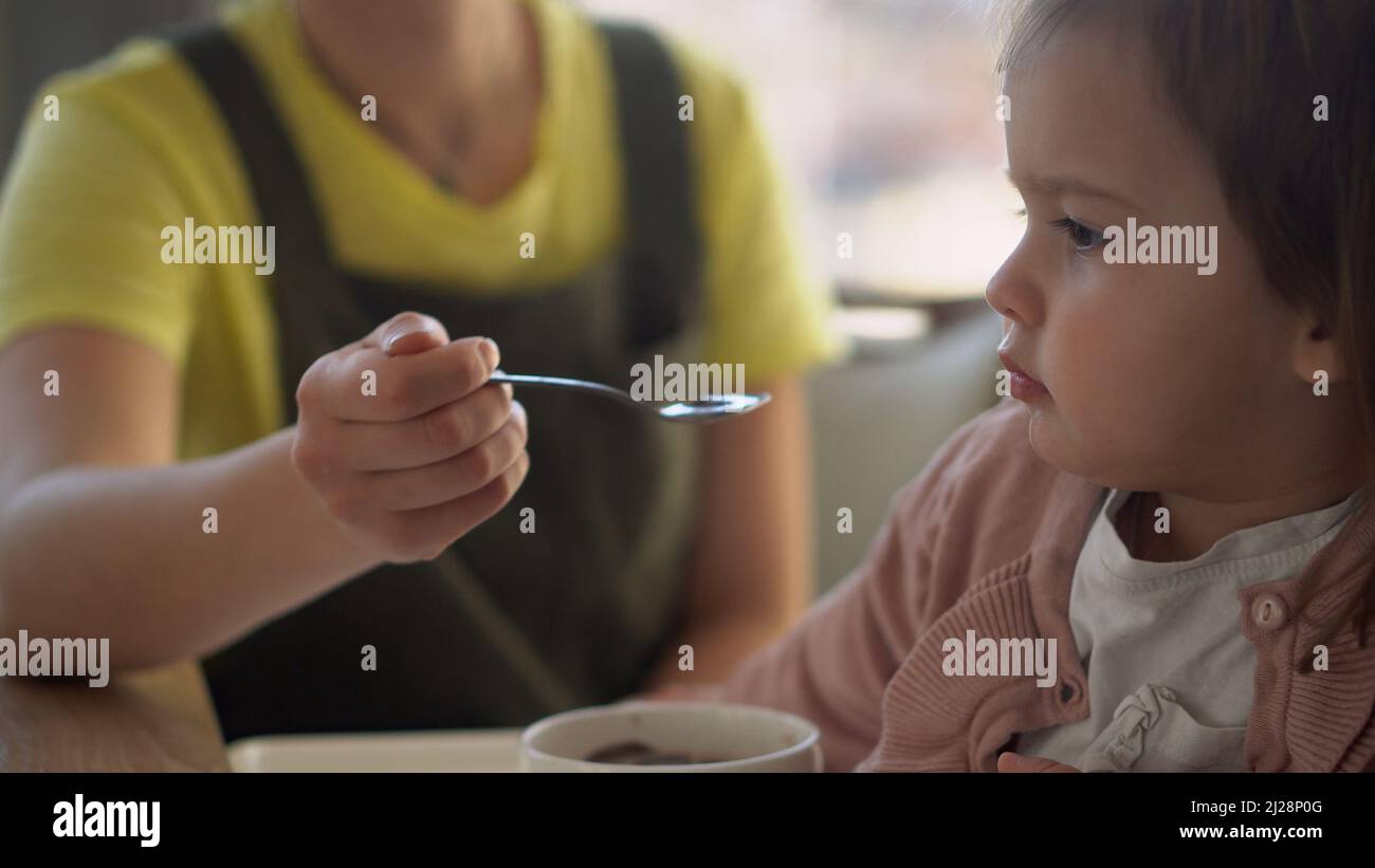 Closeup mom feed young baby in white feeding up high chair, kid is ...