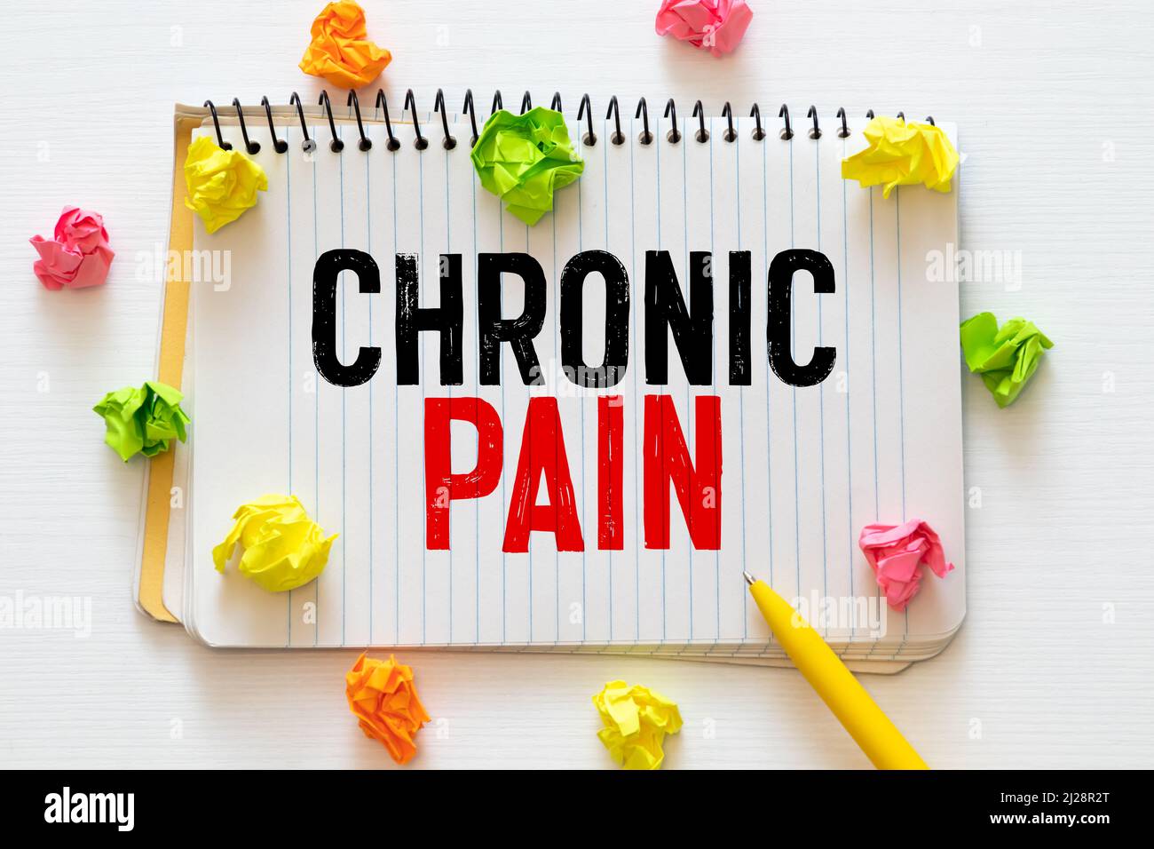 CHRONIC PAIN is written in a white notebook on a wooden table near a ...
