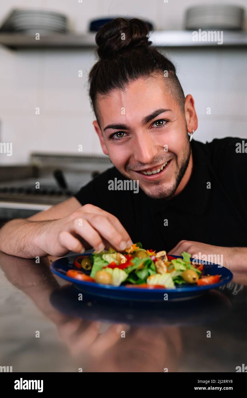 portrait of a young chief man, putting ingredients on a salad plate in ...