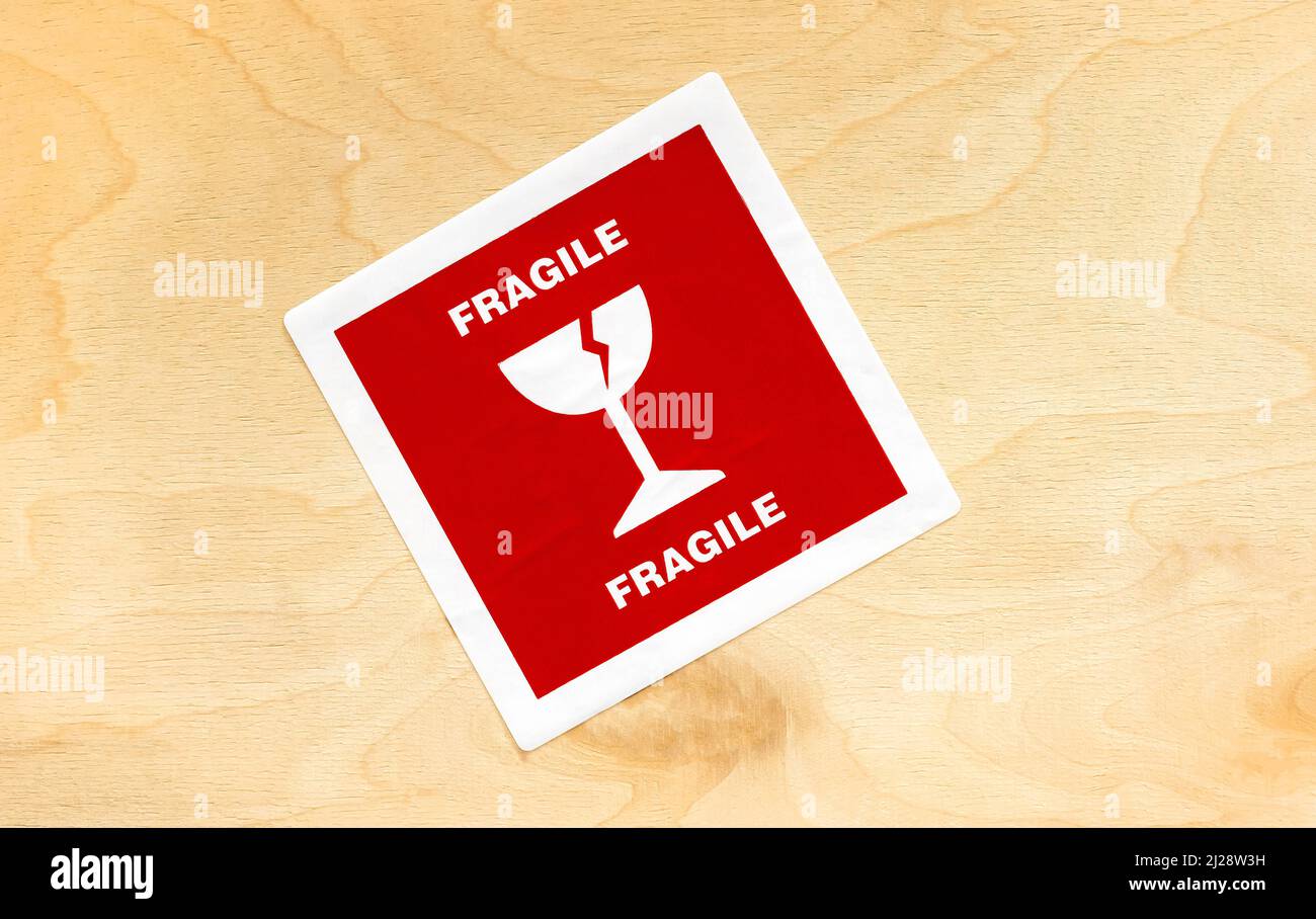 Red fragile cargo package sticker label on a wooden box crate container, detail, closeup, top ...