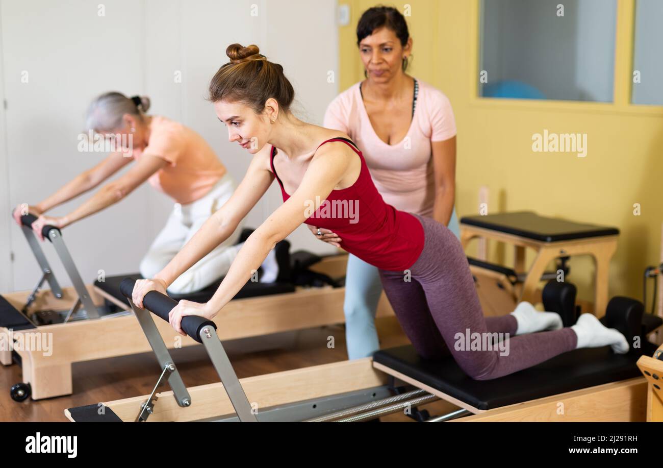 Female trainer controlling young woman doing pilates on reformer Stock ...