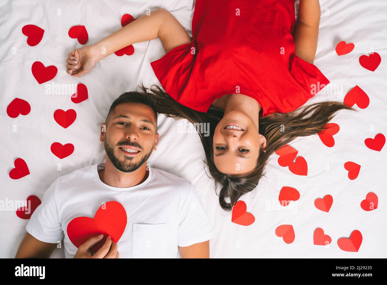 Top view of happy young couple in love with red paper hearts lying on ...