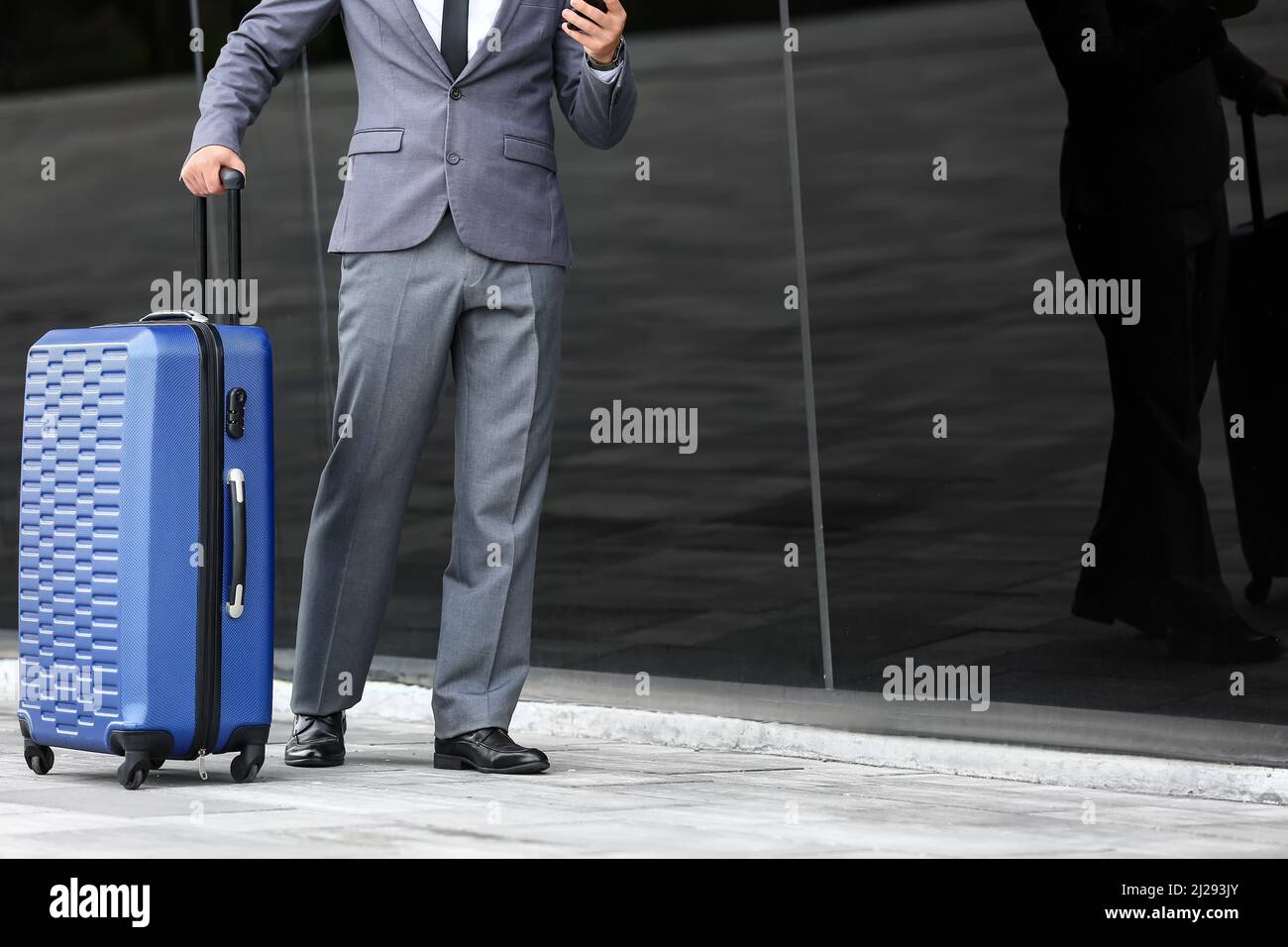Young businessman with blue suitcase using mobile phone outdoors Stock ...