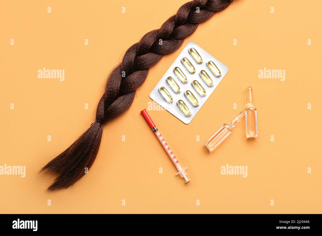 Braided hair strand with pills, syringe and ampules on orange ...