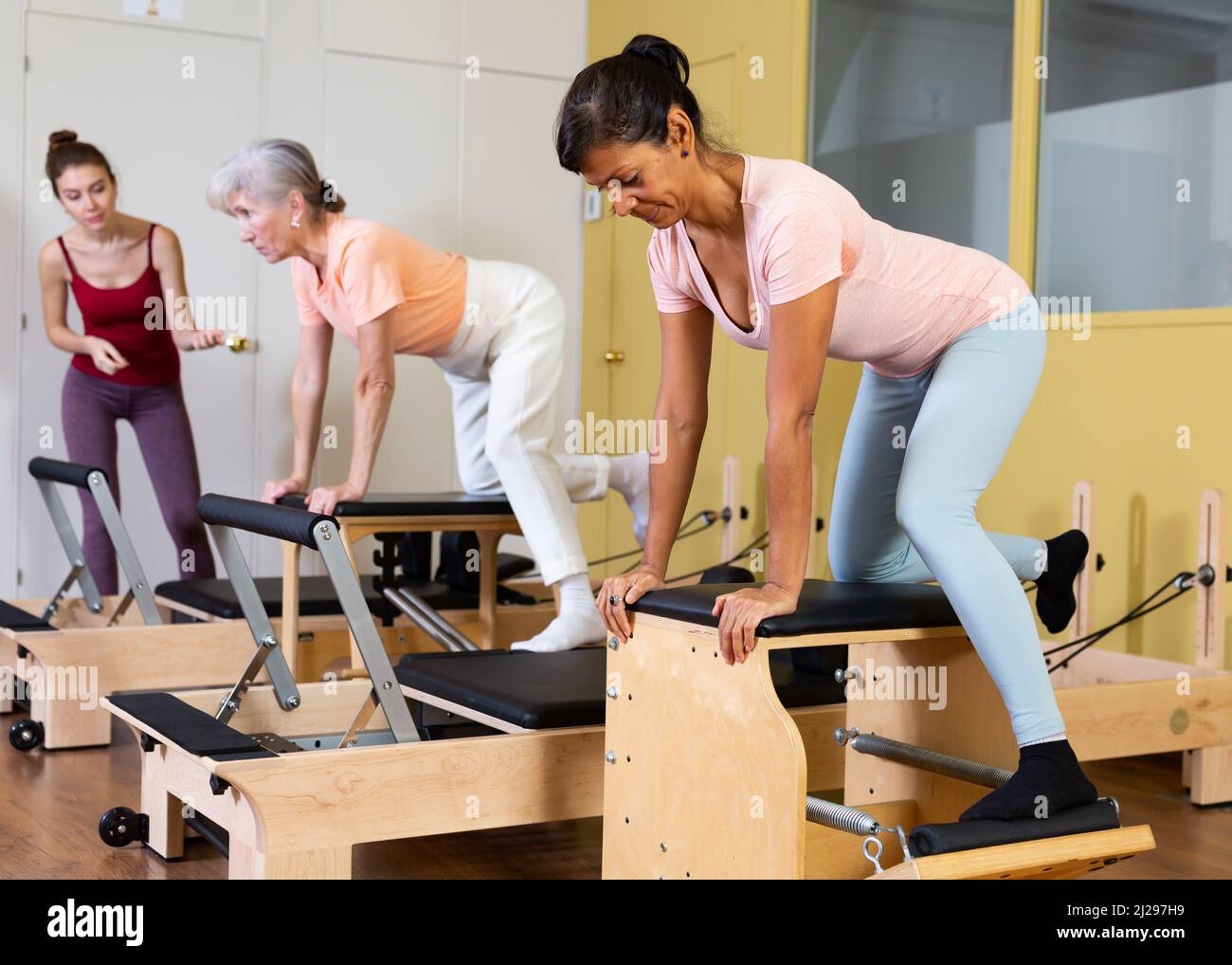Female instructor helps women perform an exercise on a combined chair ...