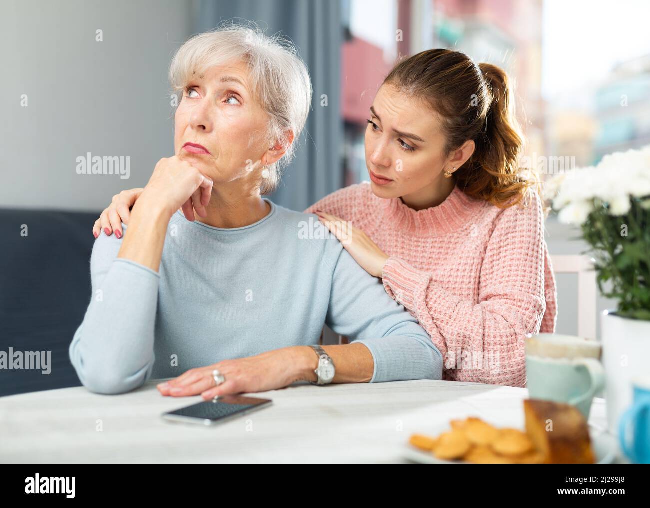 Adult daughter calming upset mother after quarrel at table Stock Photo ...