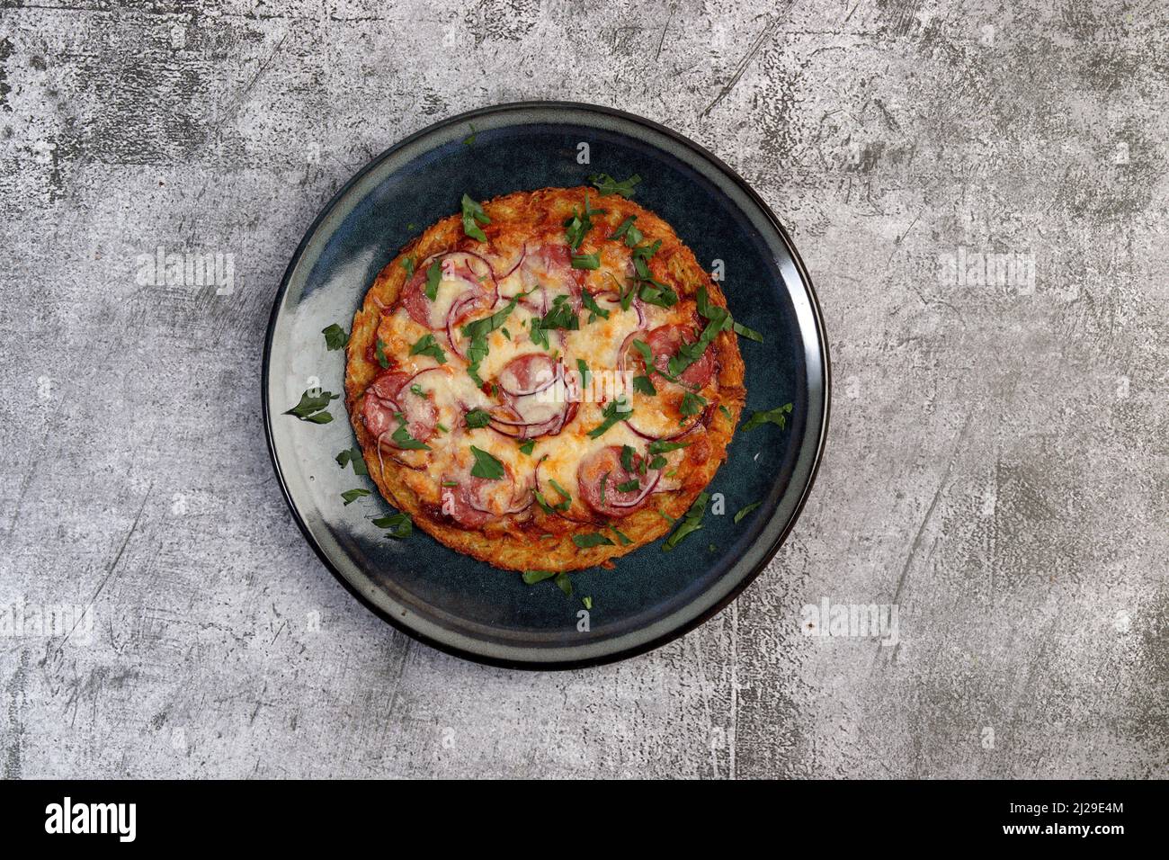 Grated Potato Crust Pizza with pink onions and salami on a round plate ...