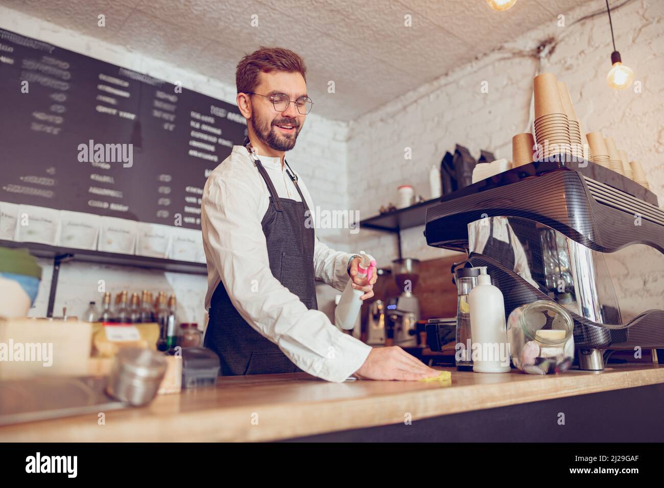 Cheerful male barista cleaning counter in cafe Stock Photo - Alamy