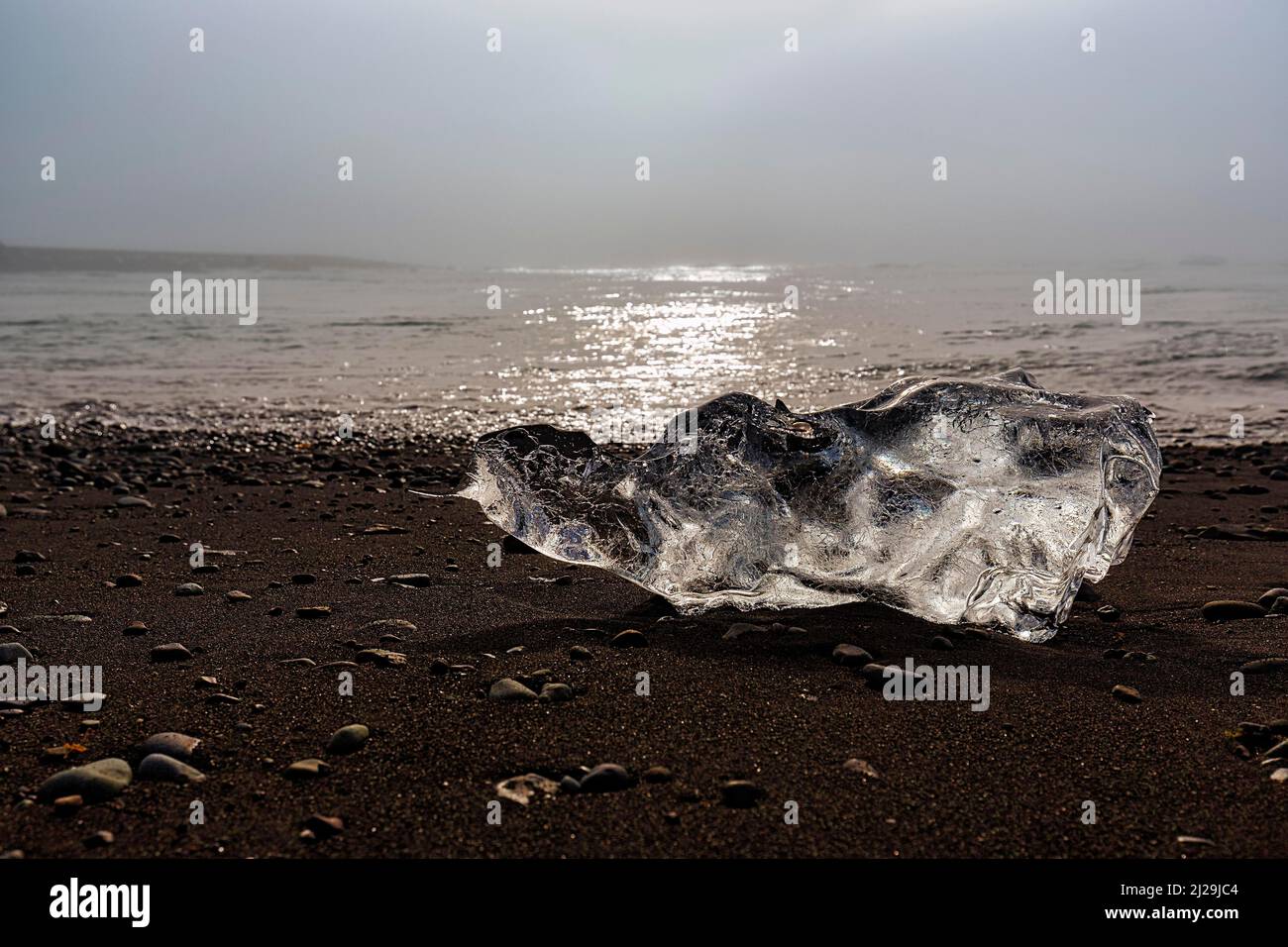 Melted iceberg, ice crystal on black lava beach, illuminated by morning ...