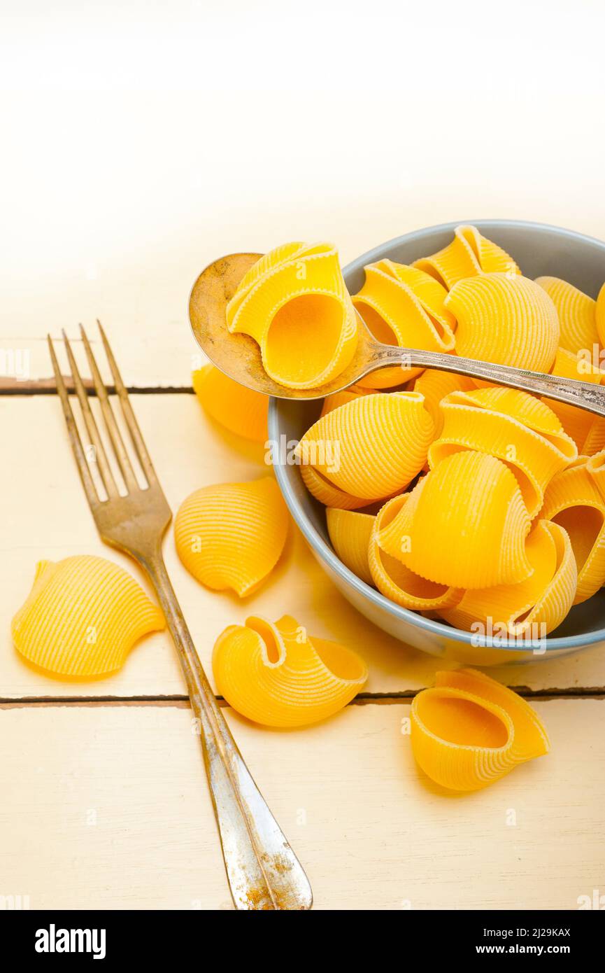 Raw Italian snail lumaconi pasta on a blue bowl over rustic table macro ...