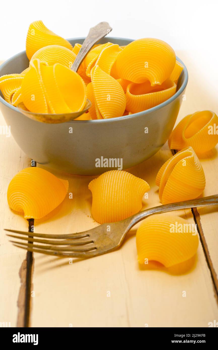 Raw Italian snail lumaconi pasta on a blue bowl over rustic table macro ...