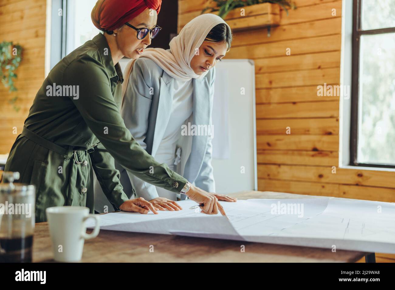 Innovative female architects working on blueprint drawings in a modern office. Two Muslim ...