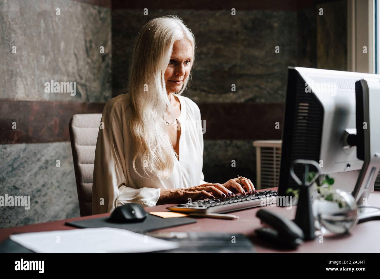 Confident female financial advisor with long white hair using computer ...