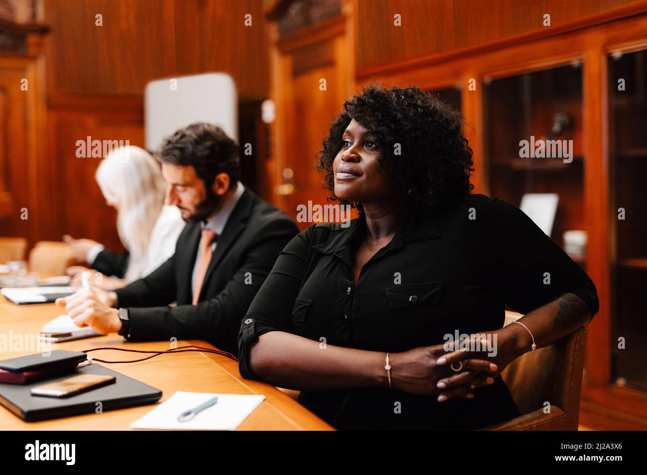 Confident businesswoman with hands clasped sitting at conference table ...