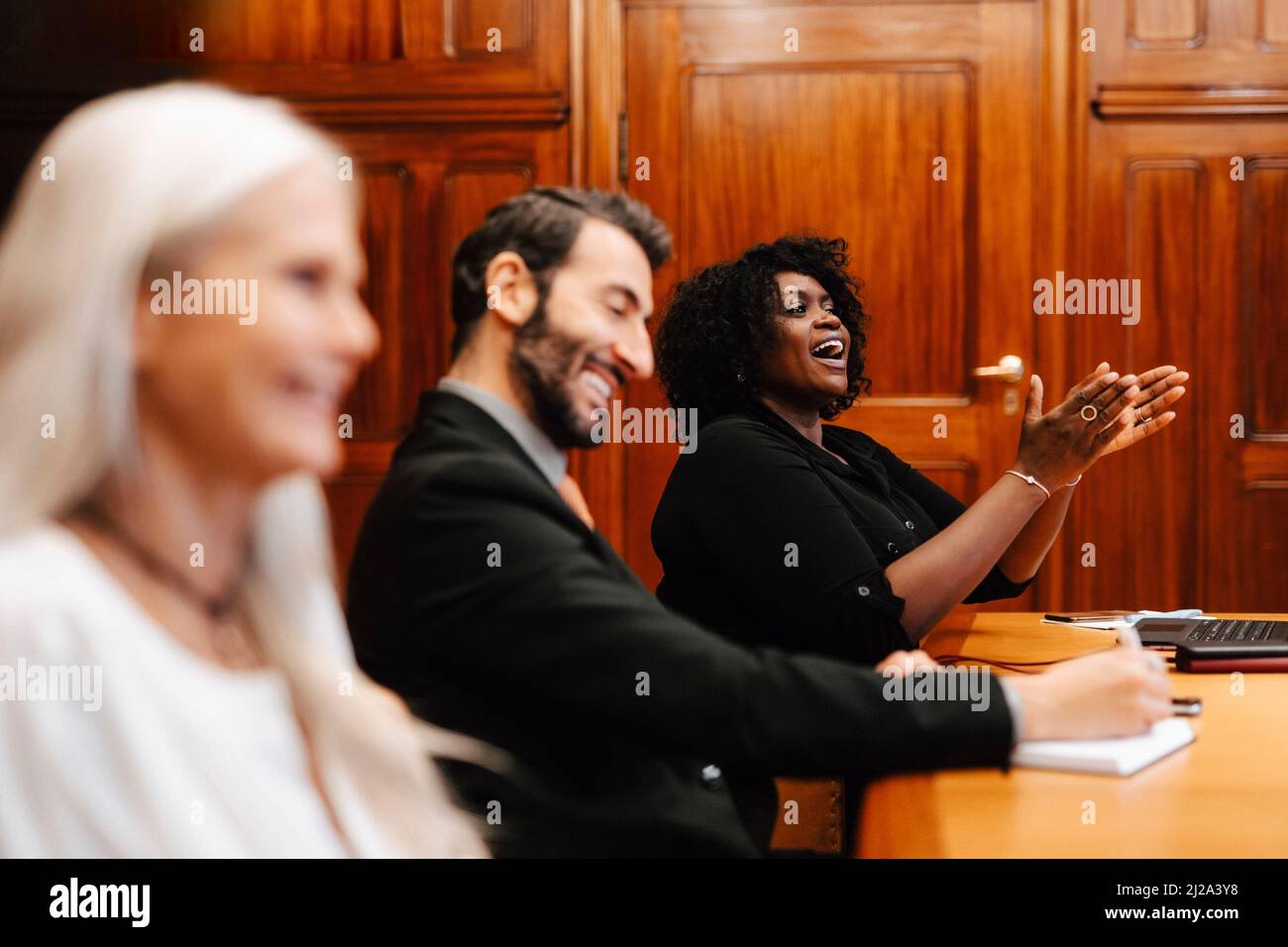 Cheerful businesswoman clapping while sitting by colleagues in board ...