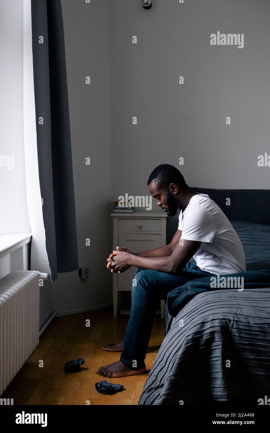 Full length side view of depressed lonely man sitting on bed at home ...