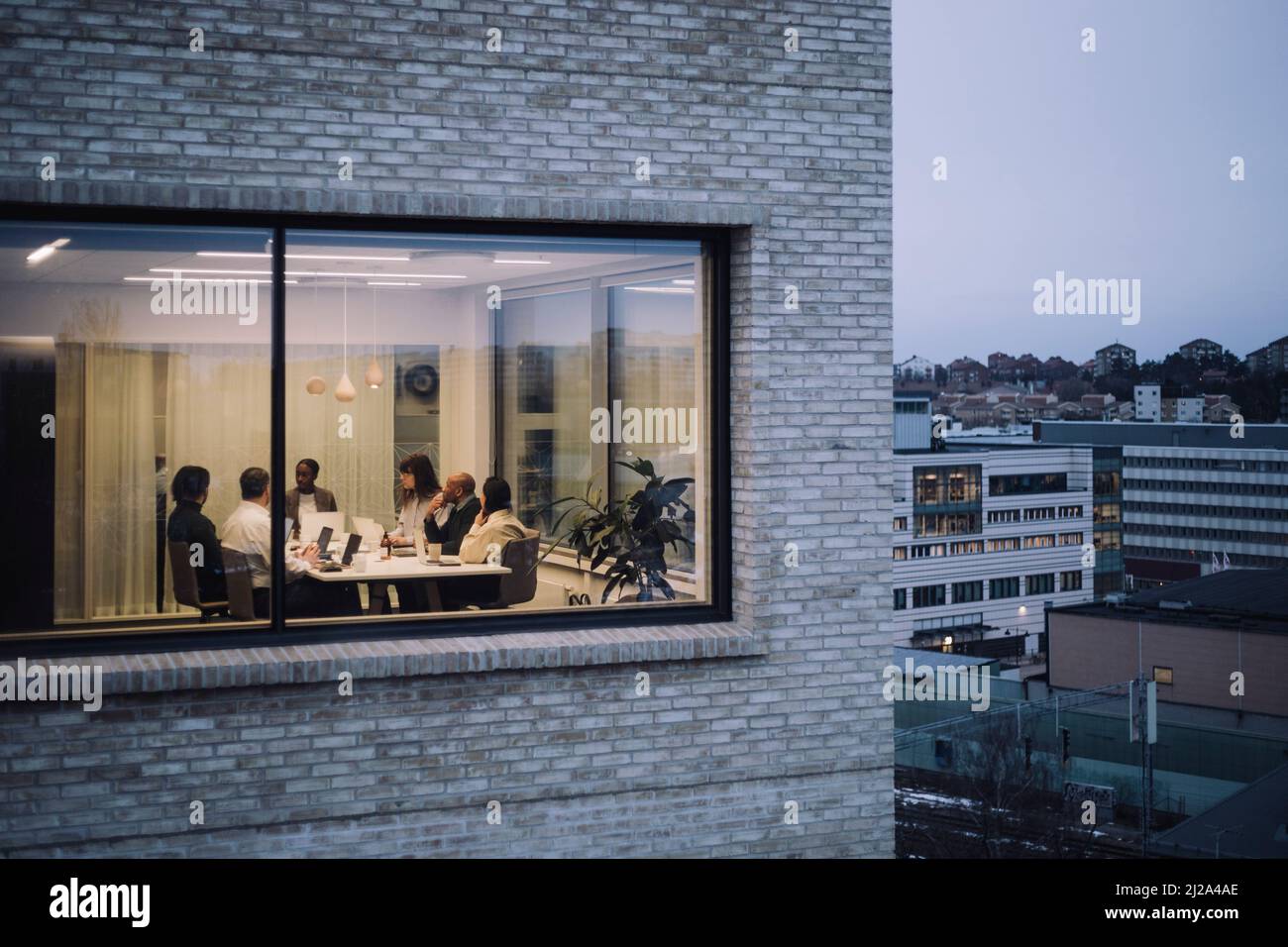 Male and female colleagues seen through window working late at work ...