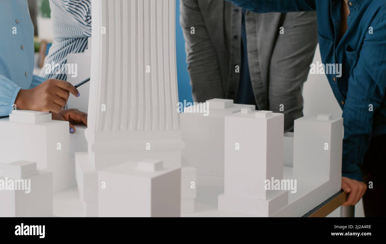Close up of team of people analyzing building model on table to plan ...
