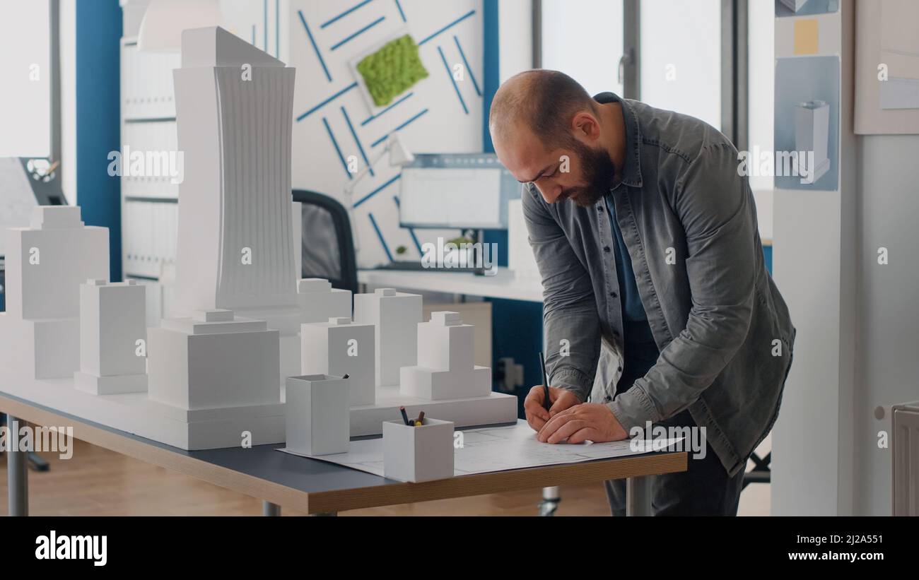 Man Engineer Analyzing Building Model To Design Blueprints Plans On Table Architect Working