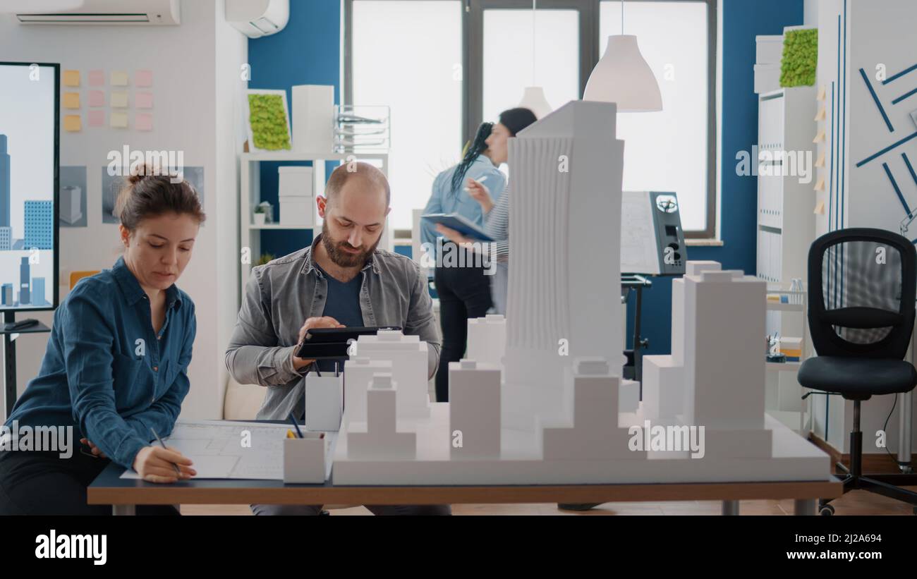 Man And Woman Analyzing Building Model And Maquette With Digital Tablet For Development Team Of