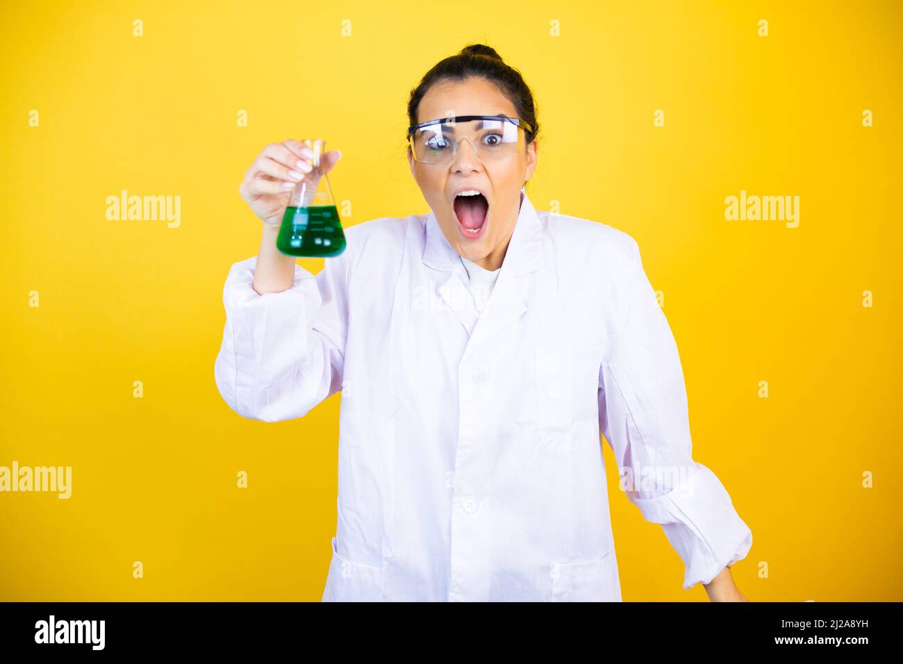 Young brunette woman wearing scientist uniform holding test tube over ...