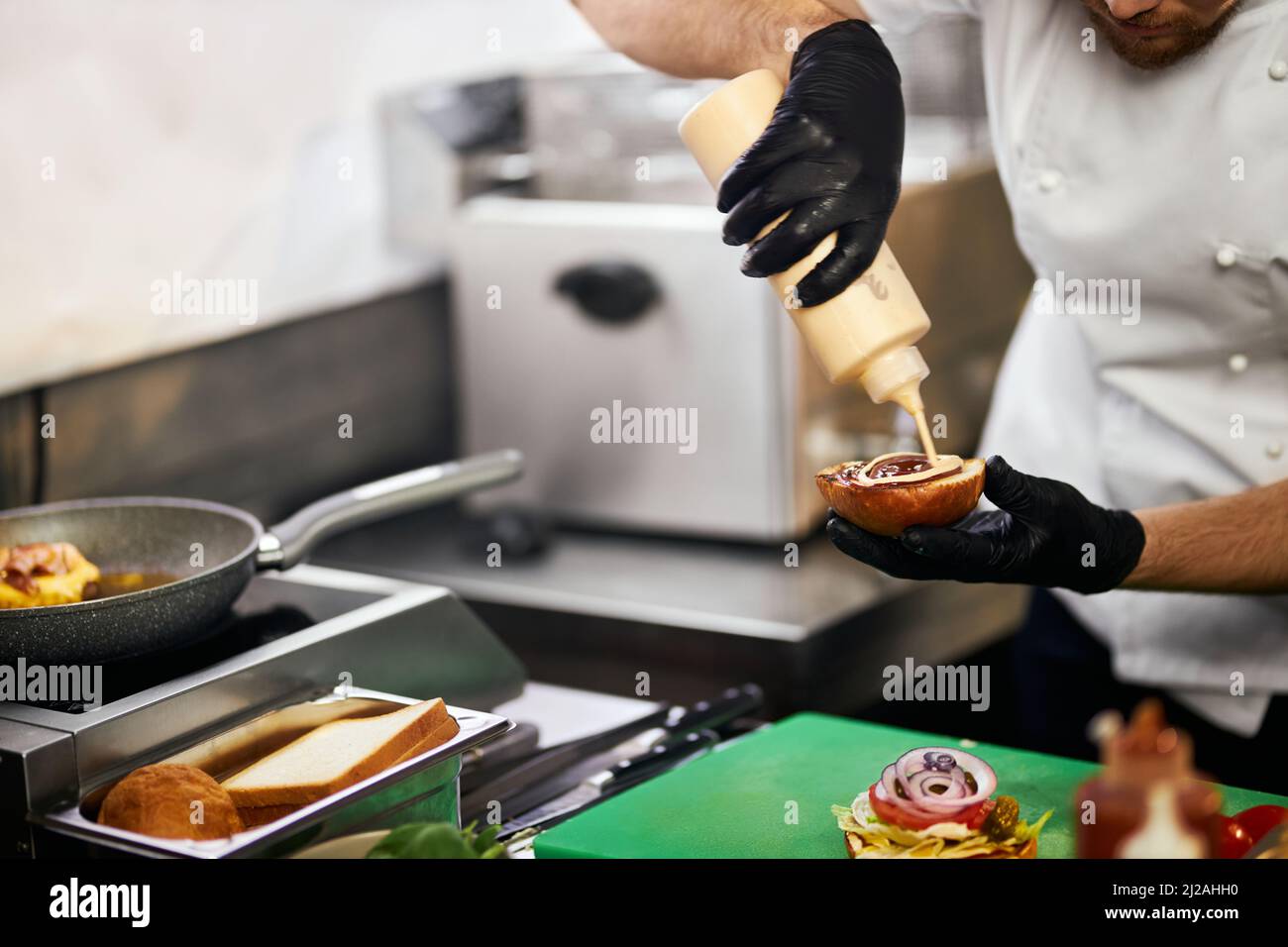 Crop view of chef's hands holding bun, pouring sauce on cheeseburger in ...