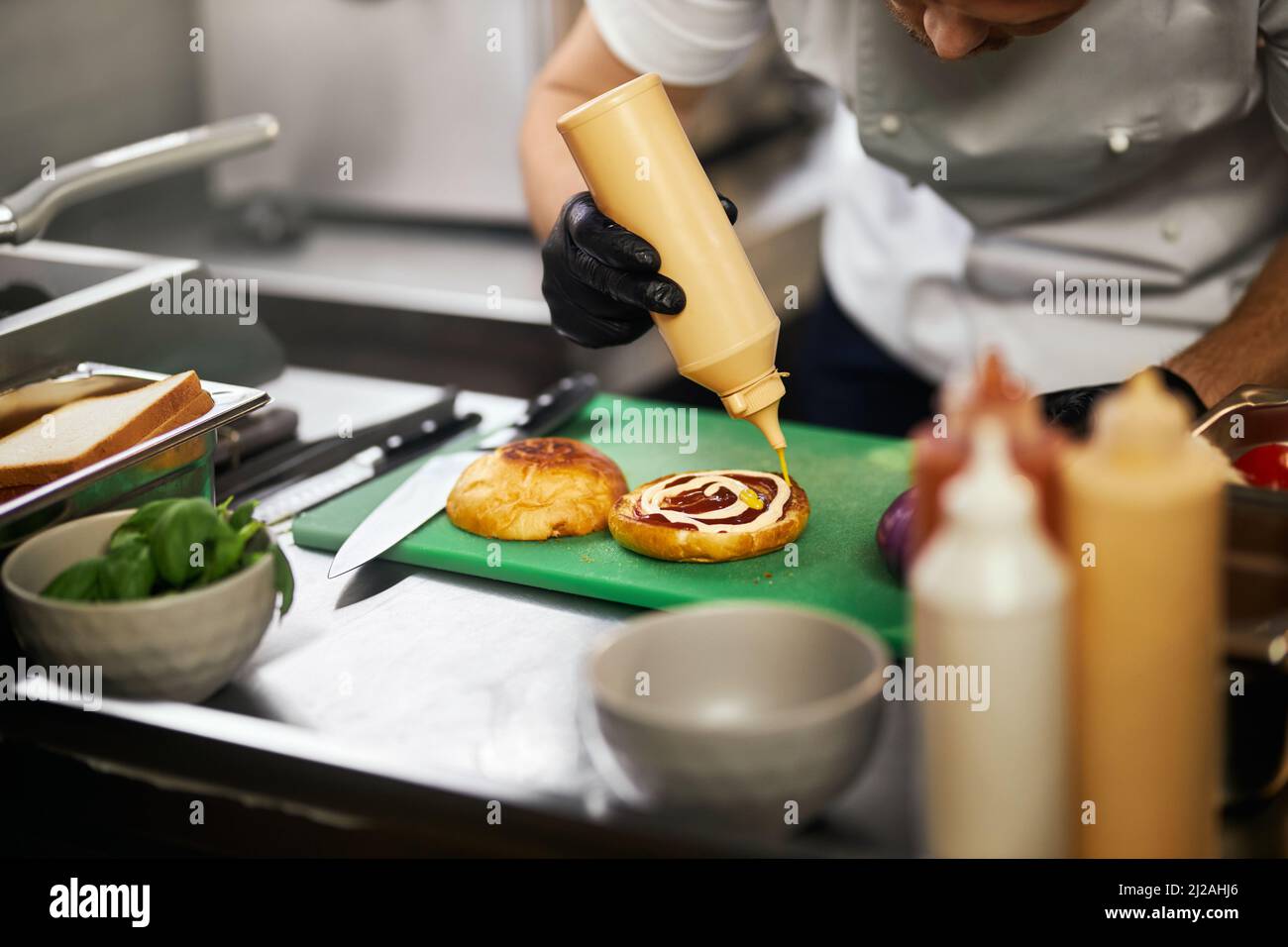 Crop view of chef's hands pouring sauce on cheeseburger in restaurant ...