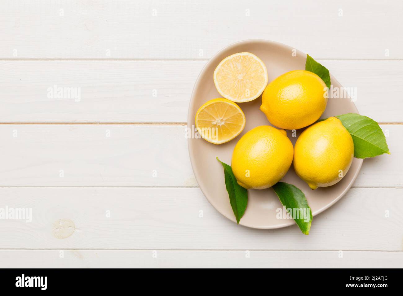 Fresh cutted lemon and whole lemons over round plate on colored ...