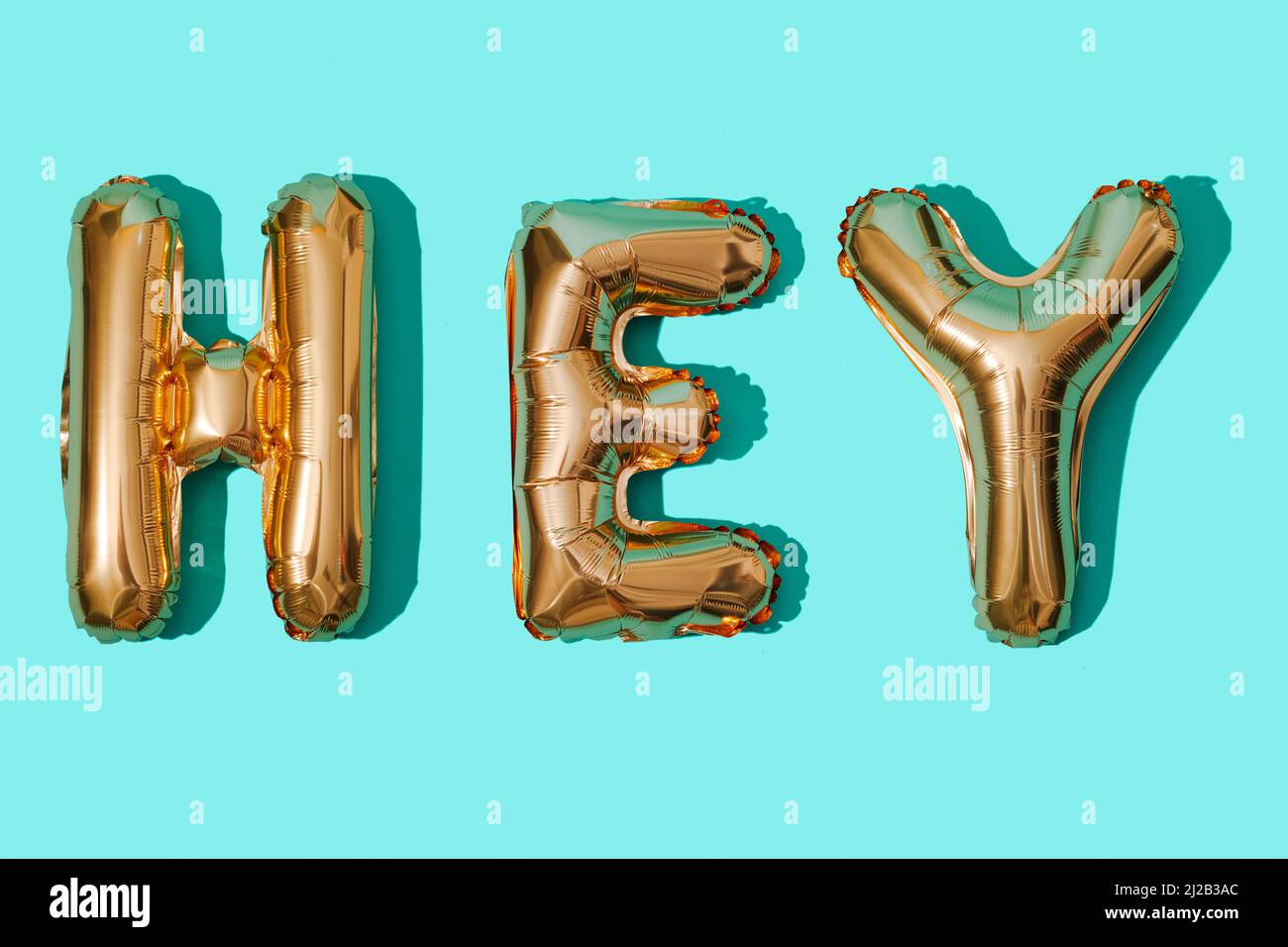 golden letter-shaped balloons forming the word hey on a blue background ...