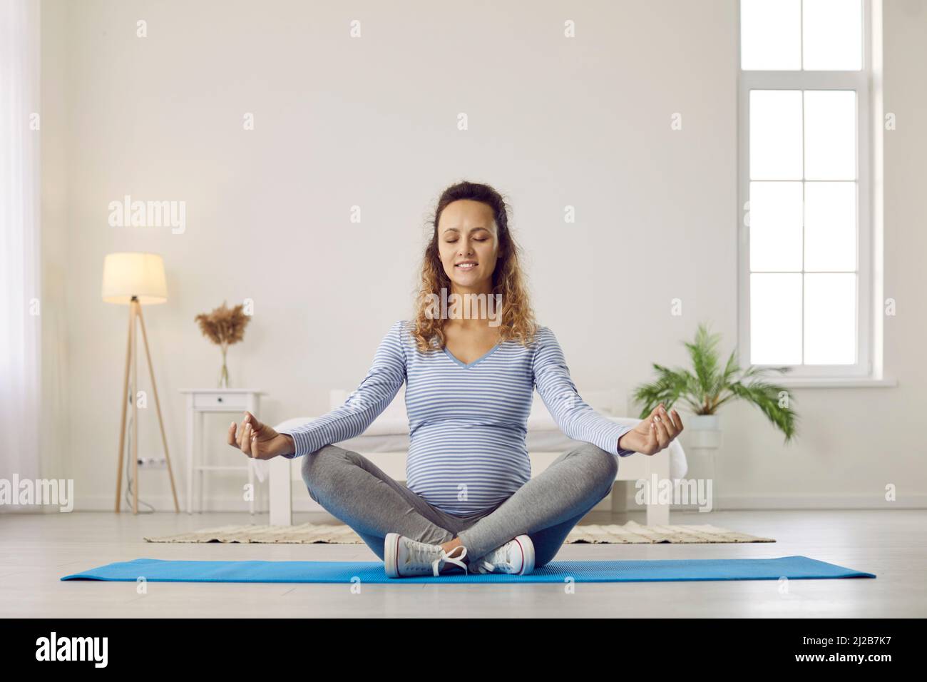 Calm pregnant woman meditates sitting in padmasana yoga position on ...