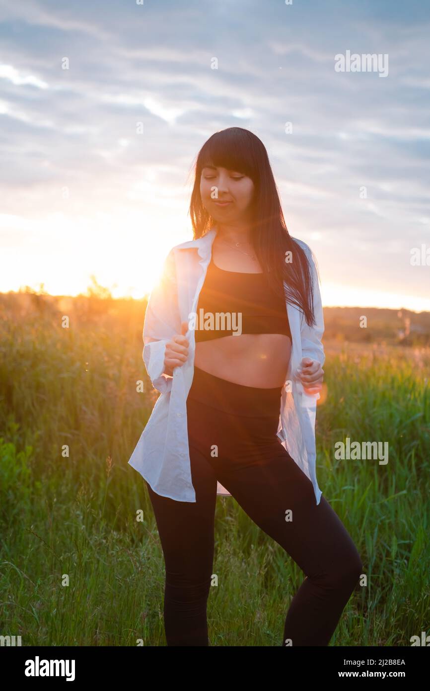 pretty young woman in white blouse on summer green field on sunset. happy peaceful time ...