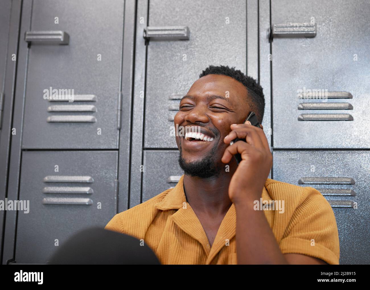 A young black student laughs on a phone call in front of campus lockers ...