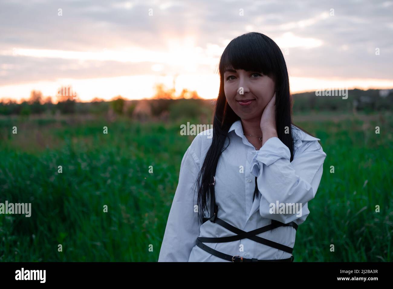 pretty young woman in white blouse on summer green field on sunset. happy peaceful time ...