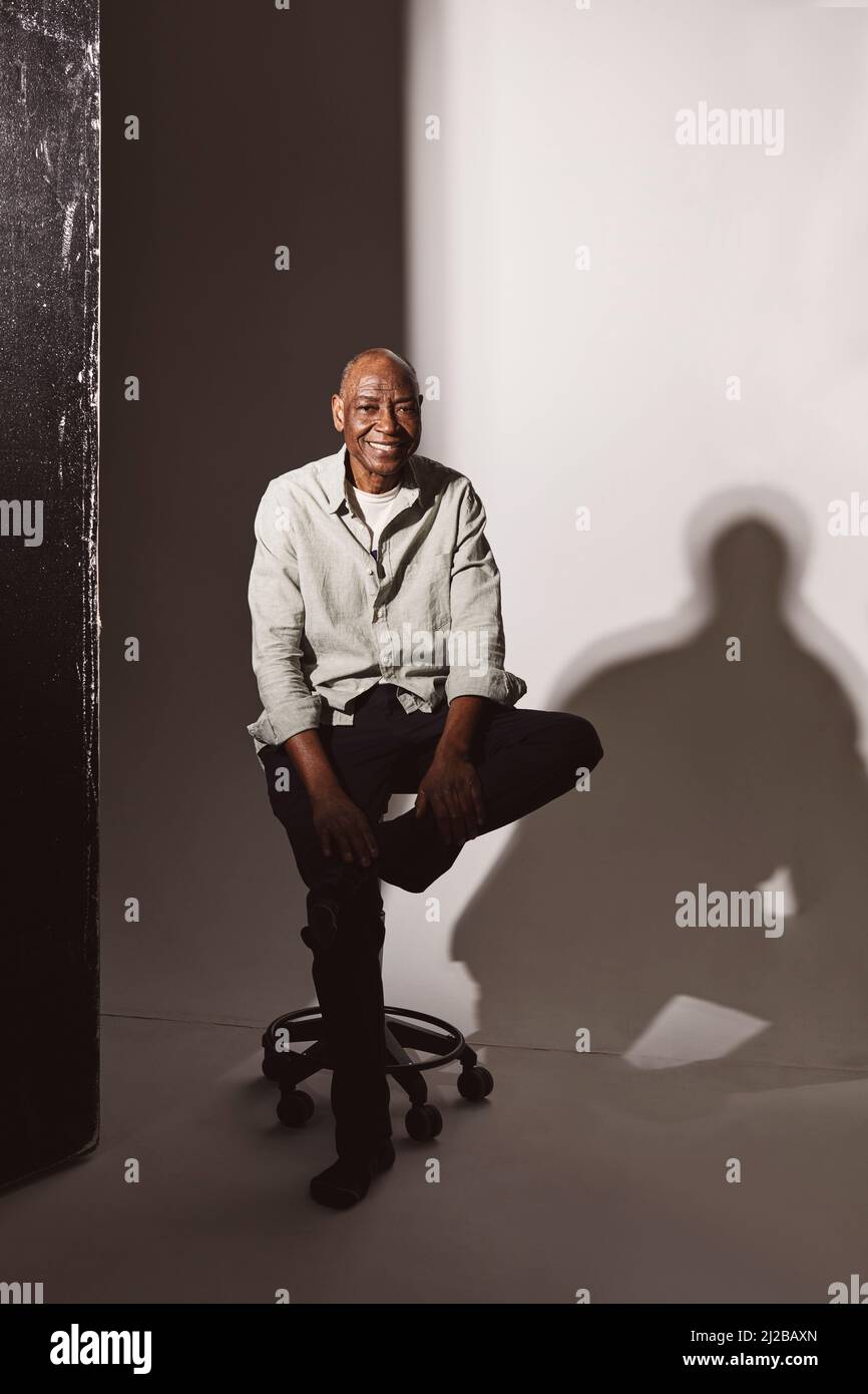 Elderly man sitting on stool against wall Stock Photo - Alamy