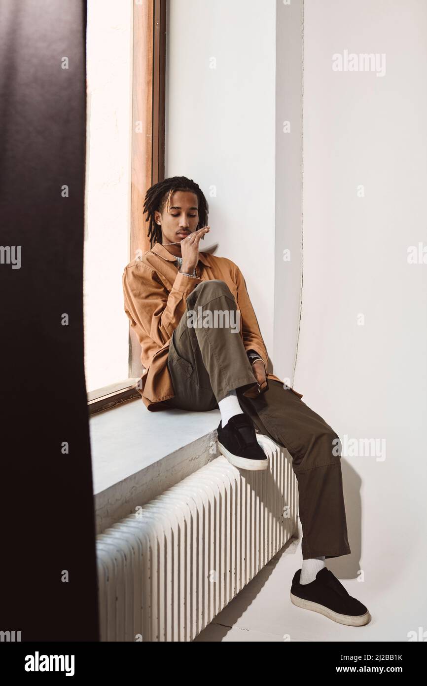 Young man sitting on window sill Stock Photo - Alamy