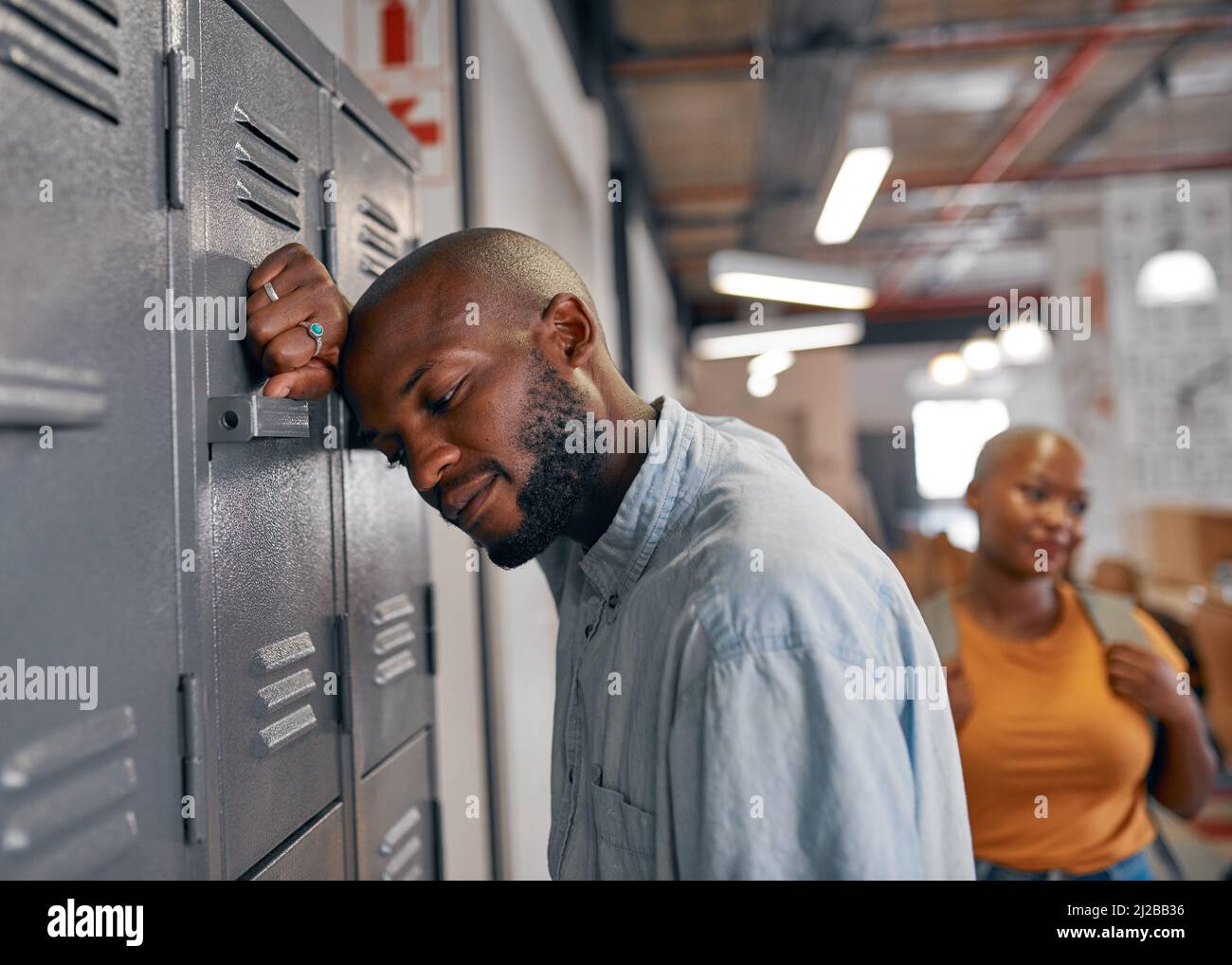 A young black student leans against locker looking stressed as friend ...