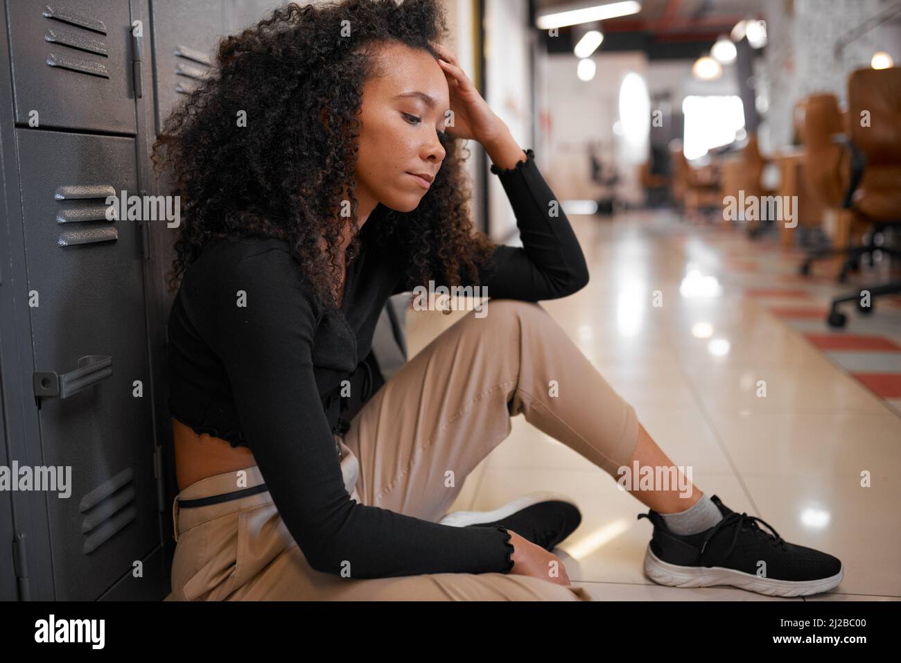 A young student sits alone in the school corridor looking unhappy and ...