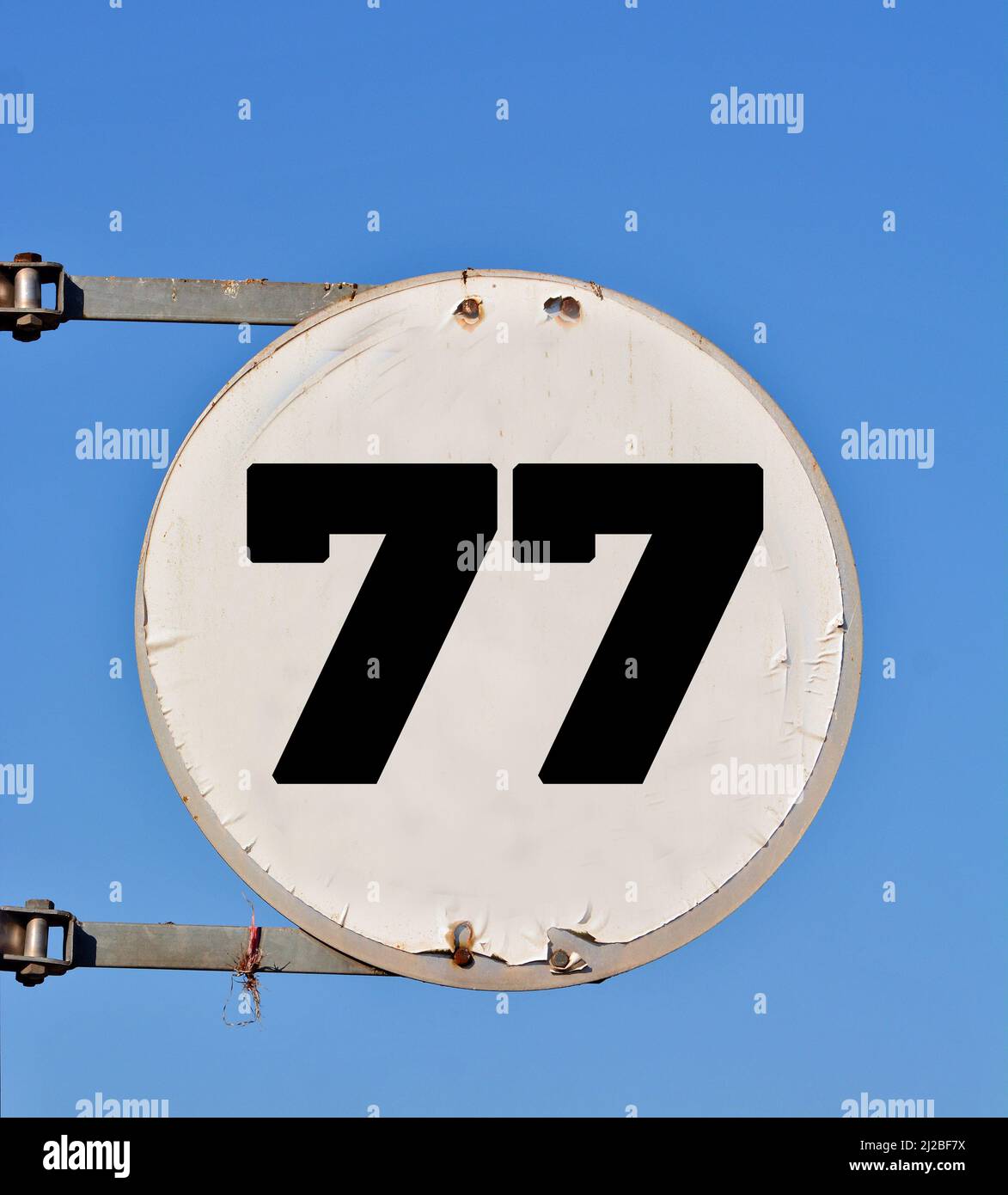 A speed limit sign with number 77 added on it against a blue sky Stock ...