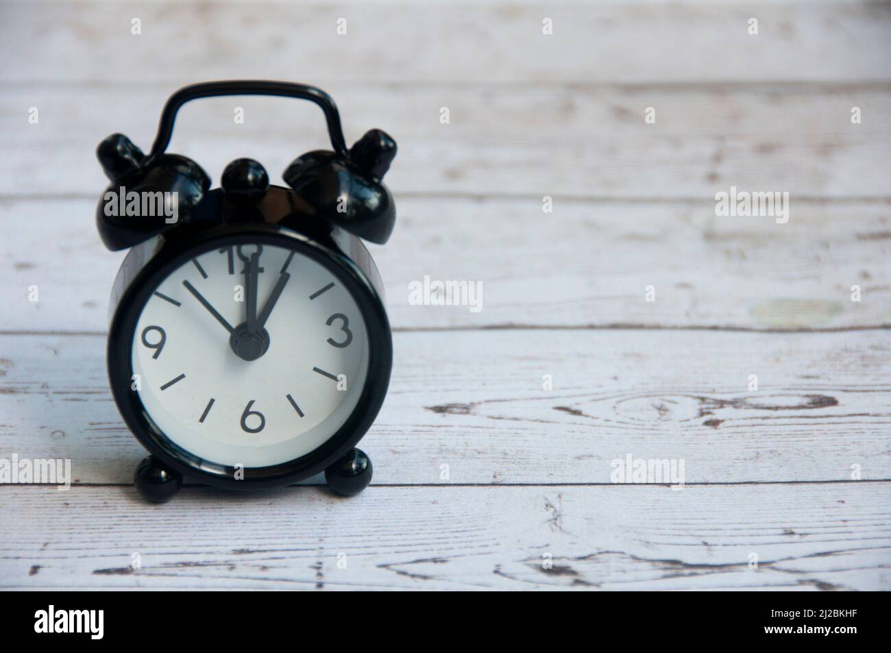 Black alarm clock isolated on wooden desk. The clock set at 1 o'clock ...