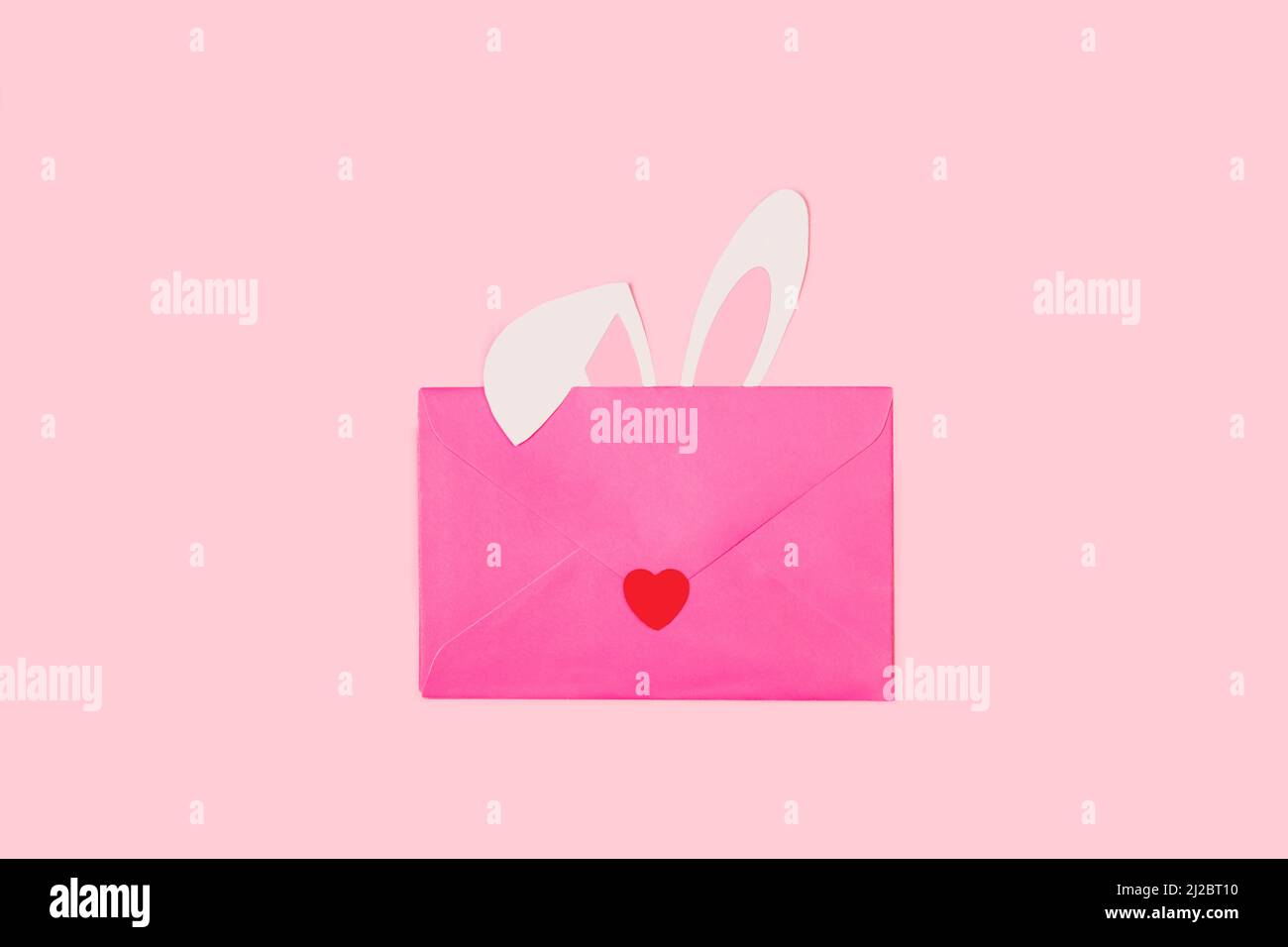 Paper rabbit ears behind of a pink envelope on a pink background with ...