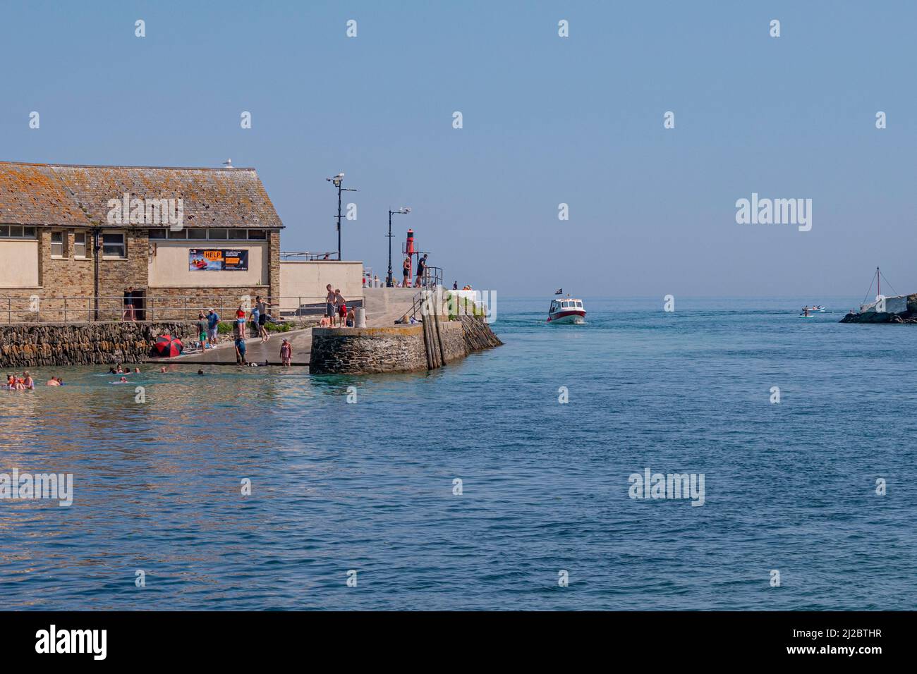 A pleasure boat enters the East Looe river from the sea, passing by the ...