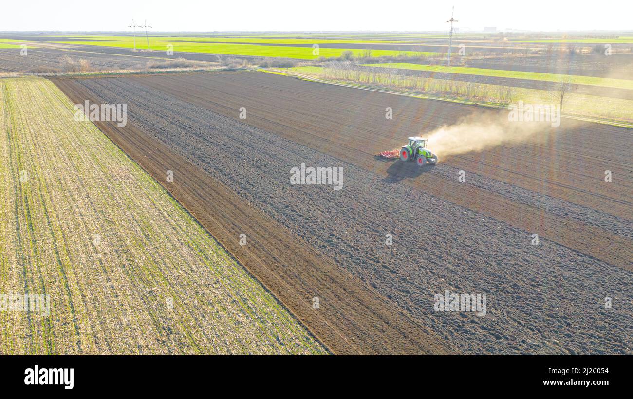 Above view of tractor as pulling machine, harrowing arable field ...