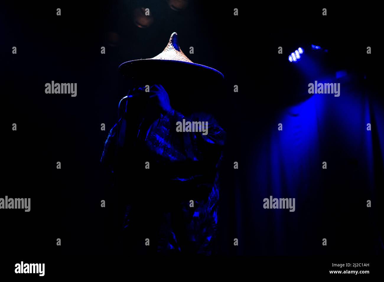 An African singer in an asian hat performing live on a stage with blue ...