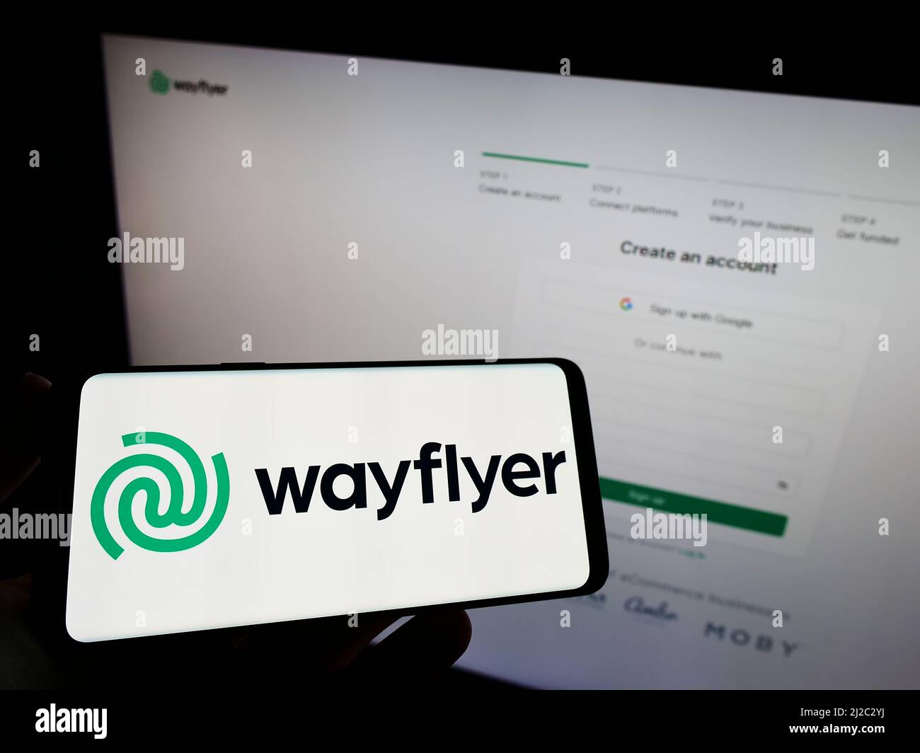 Person holding mobile phone with logo of Irish e-commerce company Wayflyer Limited on screen in ...
