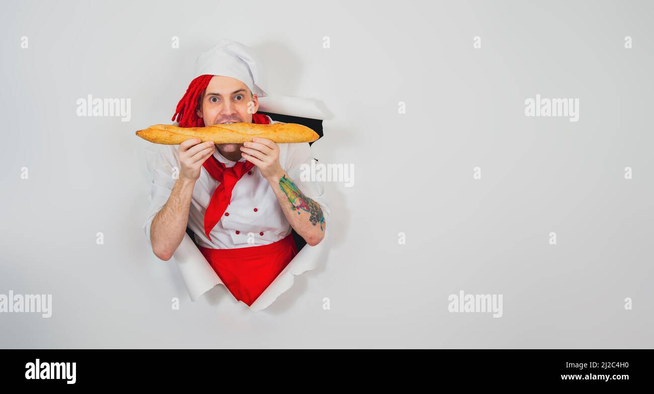 Young man with red dreadlocks dressed as chef bites white bread ...
