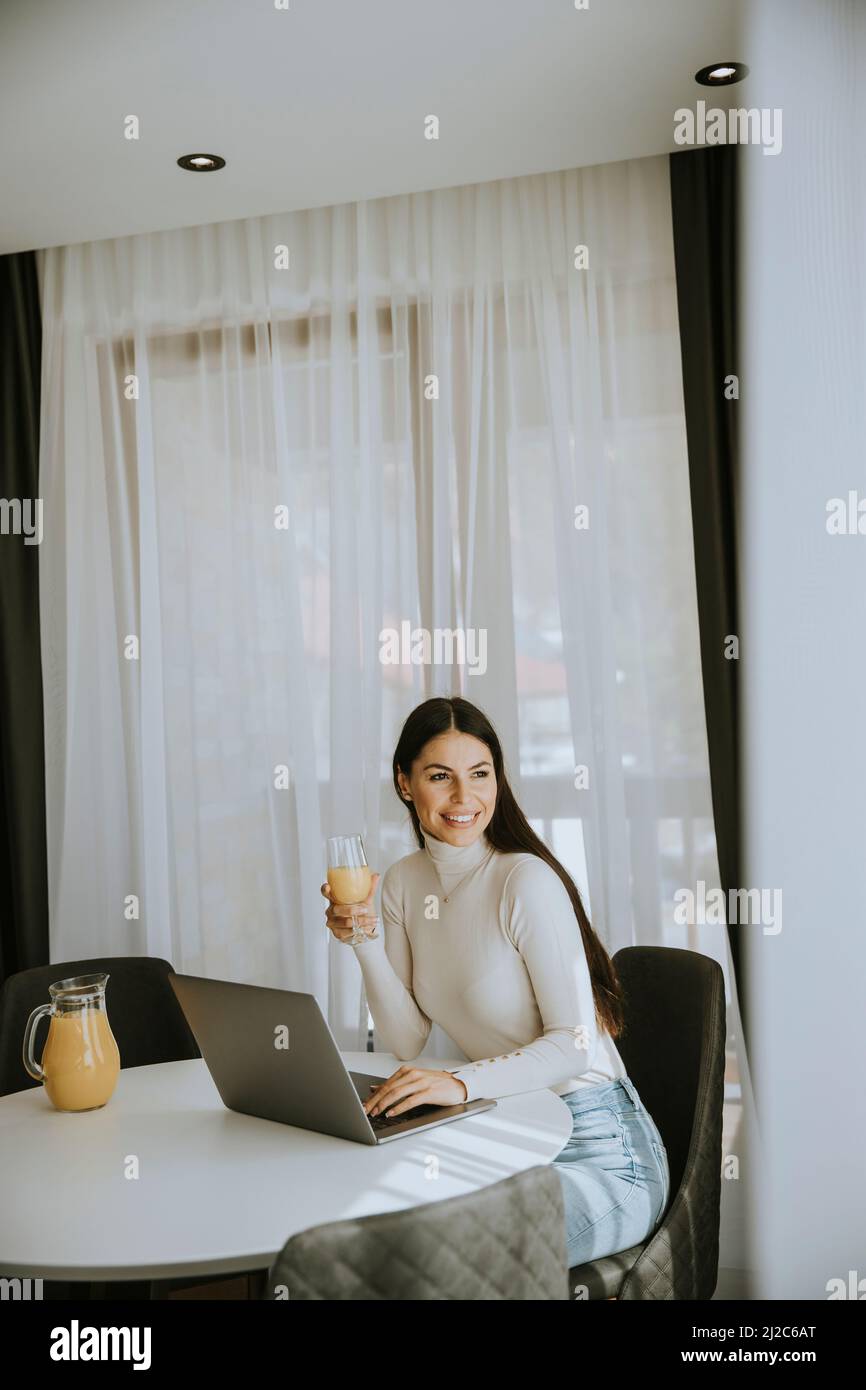 Young woman using a laptop computer and drinking healthy orange juice ...