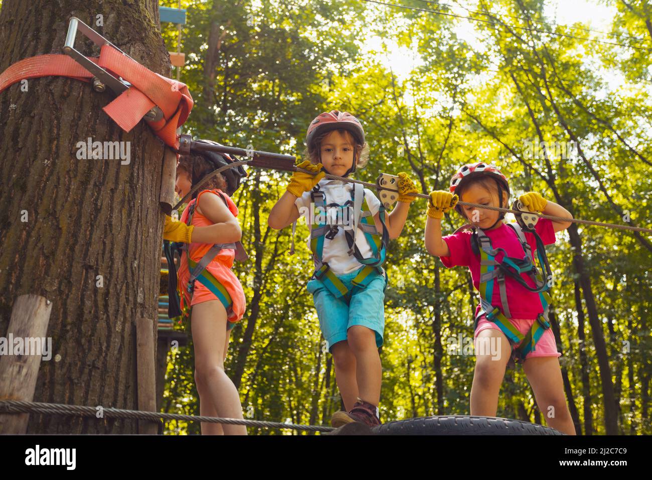The cute little kids are going one after another in the rope park. The ...