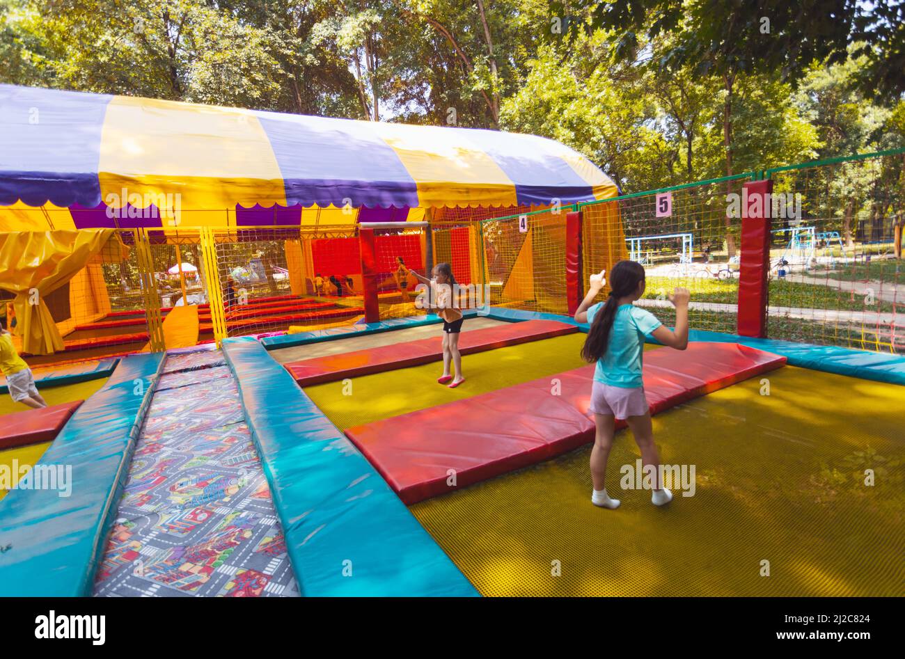 The young children are jumping in the bright trampoline park outdoors ...