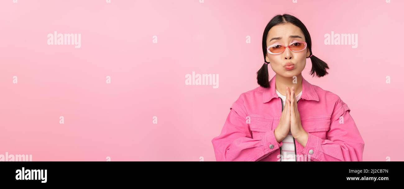 Please. Cute asian girl asking favour, begging, standing against studio ...